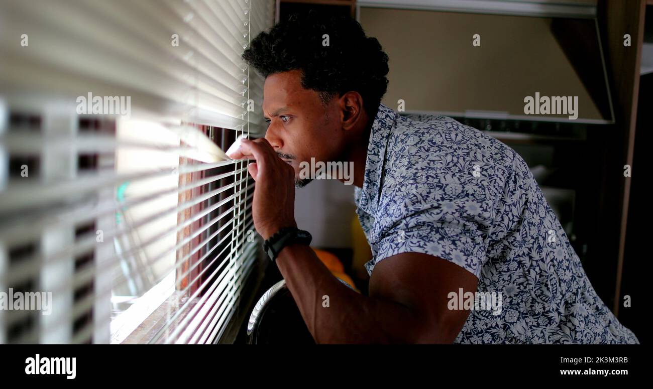 Suspicious man looking through window blinds Stock Photo - Alamy