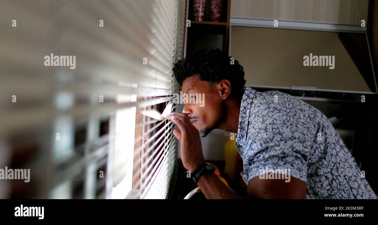Suspicious man looking through window blinds Stock Photo - Alamy