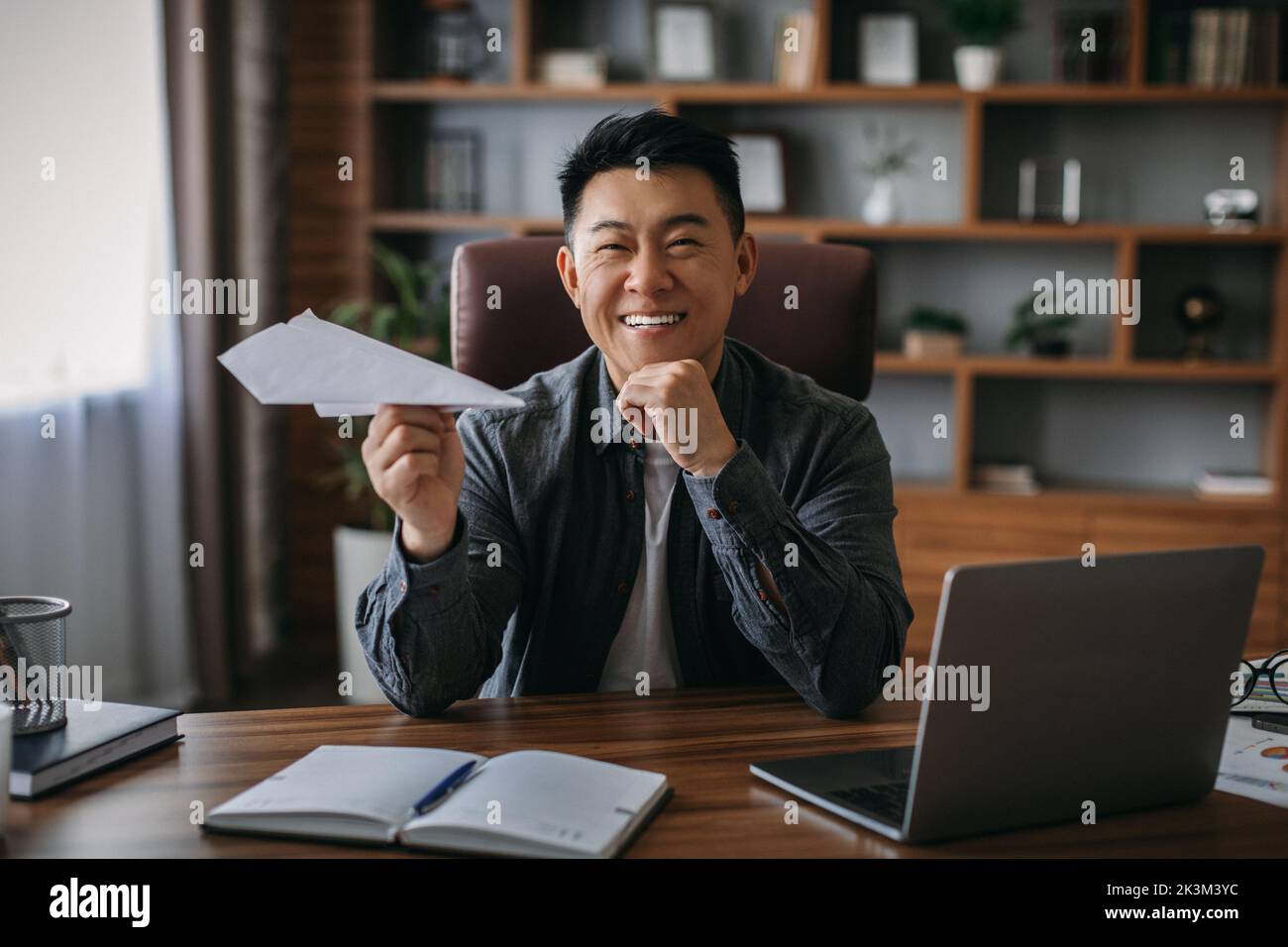 Happy adult chinese man rest from work, make paper airplane in office ...