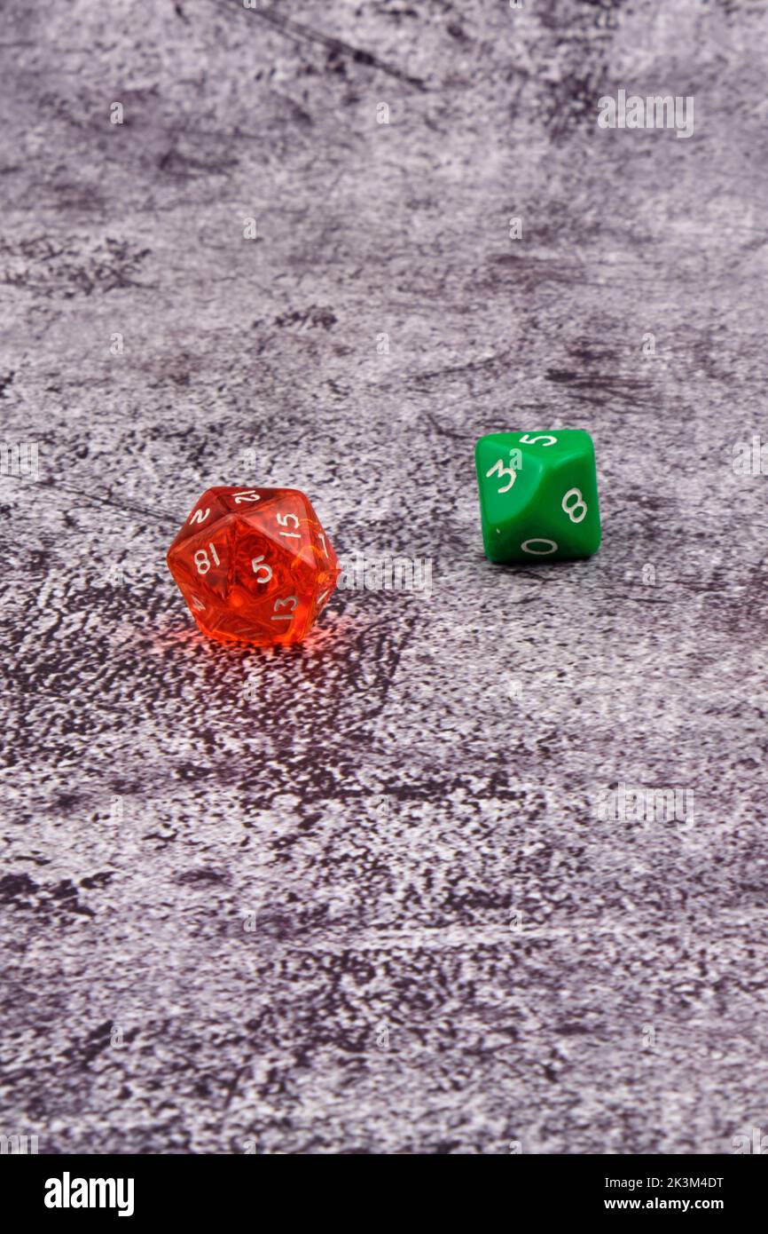 Two role-playing game dice, one red and one green, on top of a cement ...