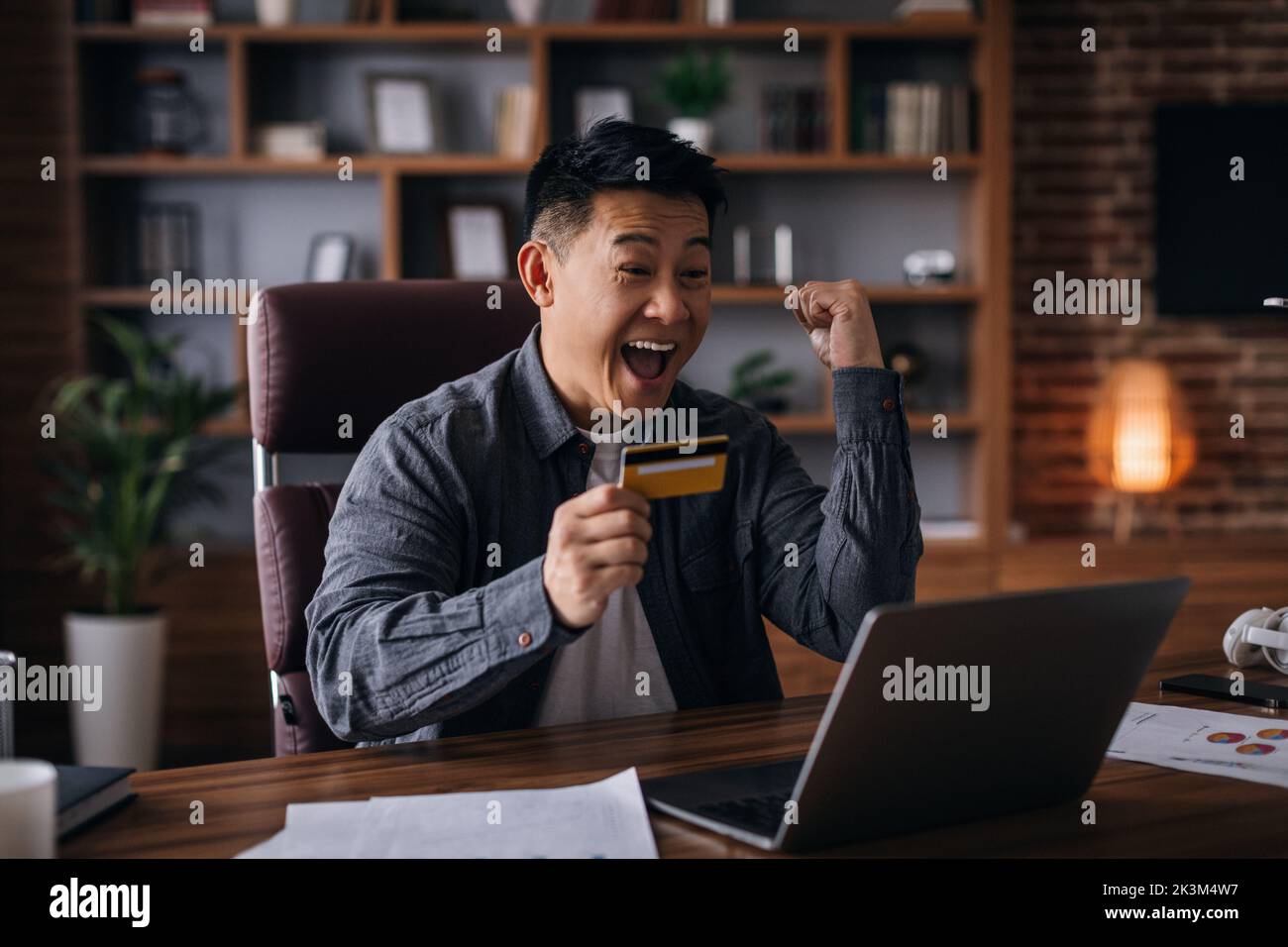 Glad adult asian man with open mouth, scream, hold credit card, looks ...
