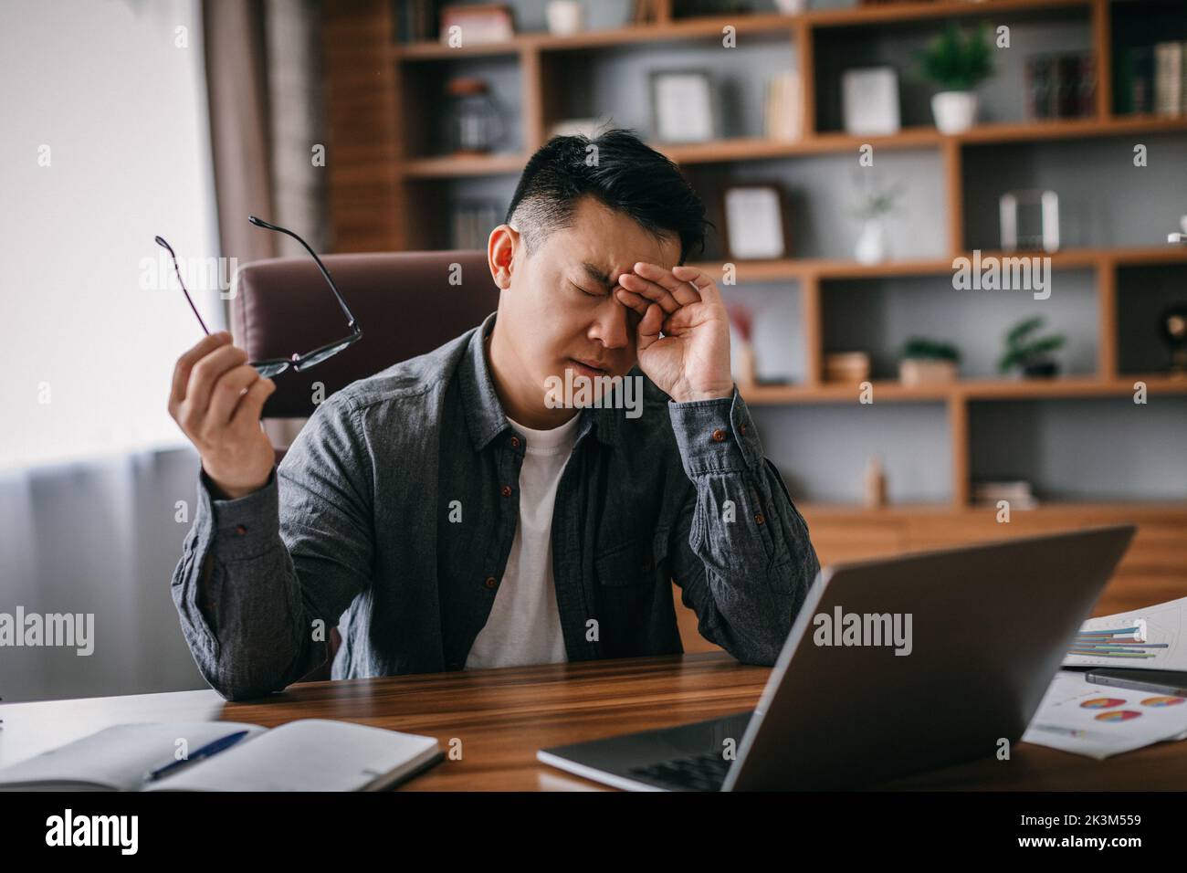 Sad tired adult chinese man takes off his glasses, rubs eyes and rests ...