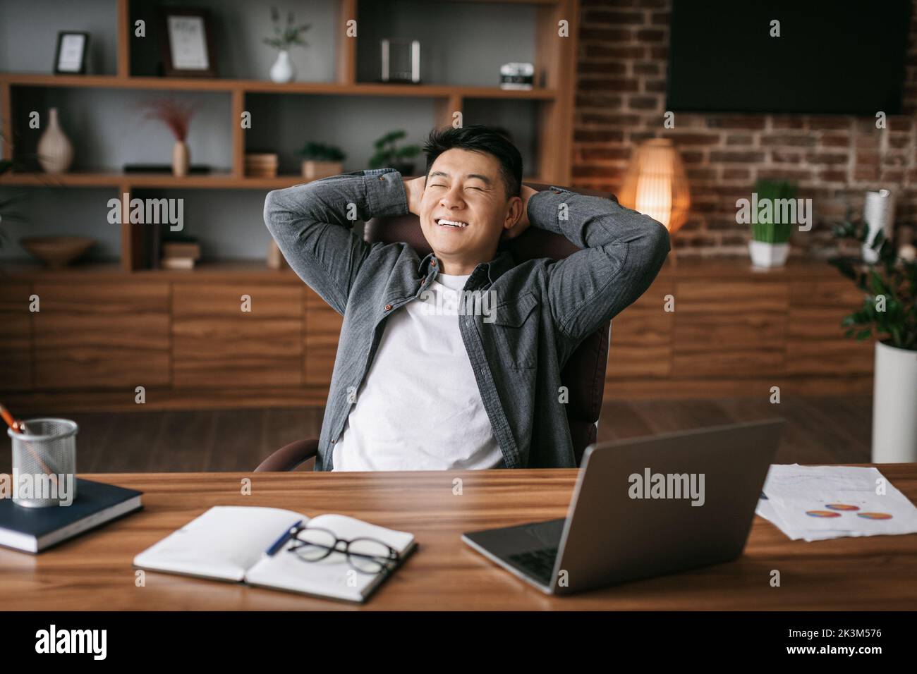 Satisfied adult japanese man resting in chair at table in office ...