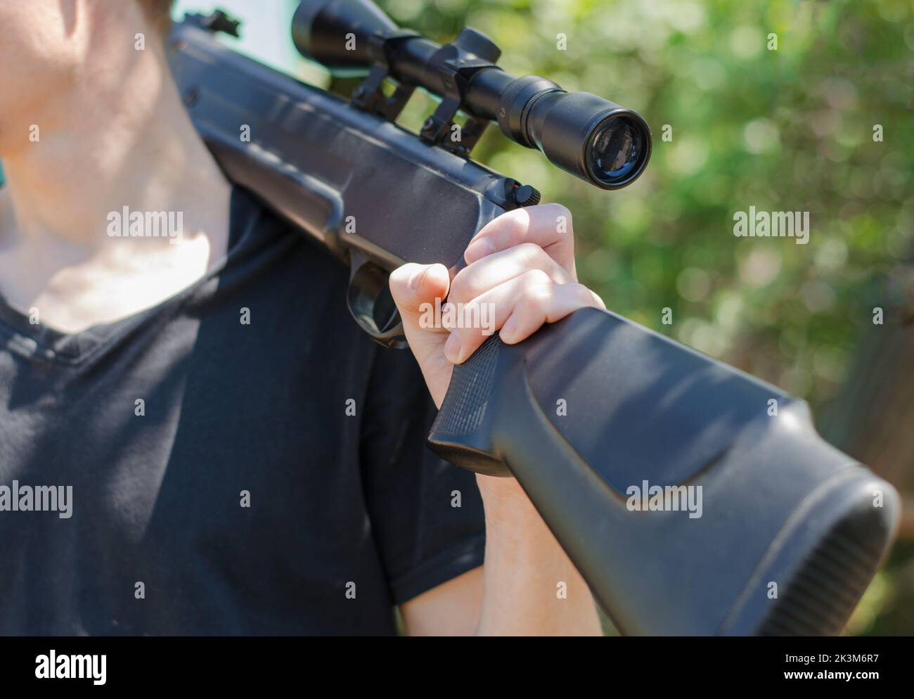 An unrecognizable man holds a rifle with an optical sight on his ...