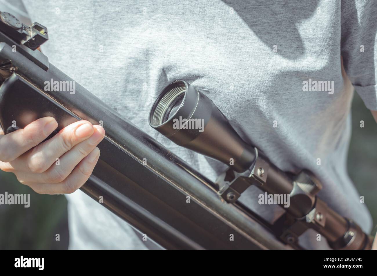 A woman is holding a large sniper rifle, close-up. A young girl with a ...