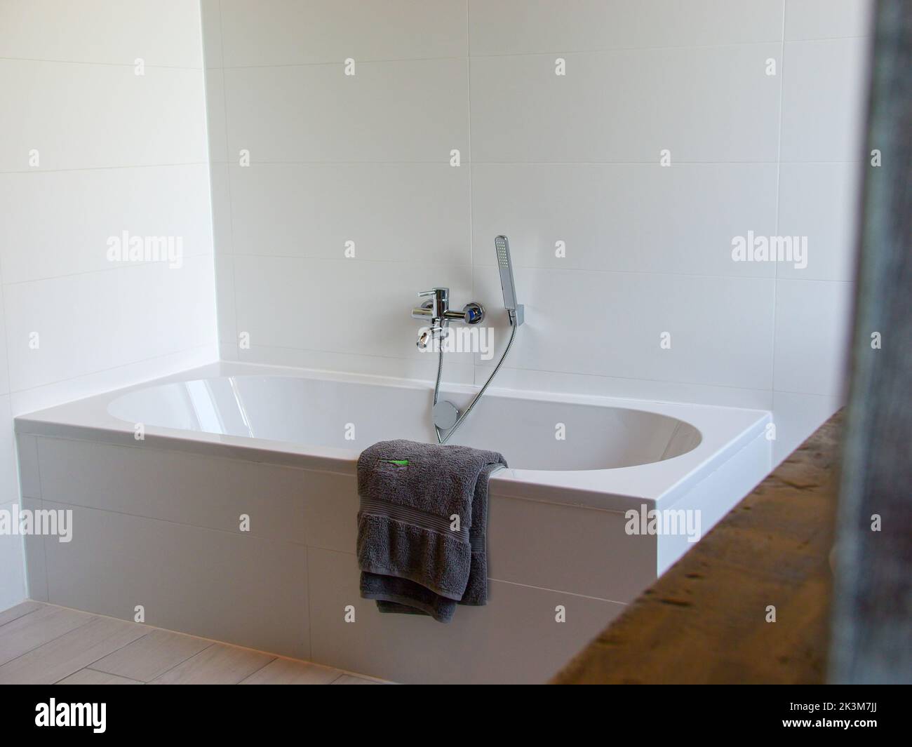 A simple white bath tub with a gray towel on the rim in a bathroom ...