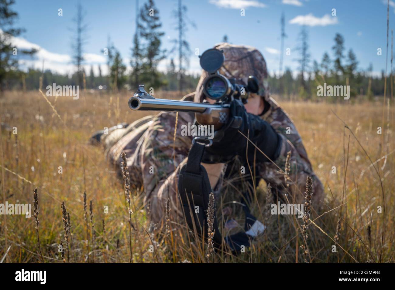 A sniper in camouflage laying on the grass hunting with a rifle in a ...
