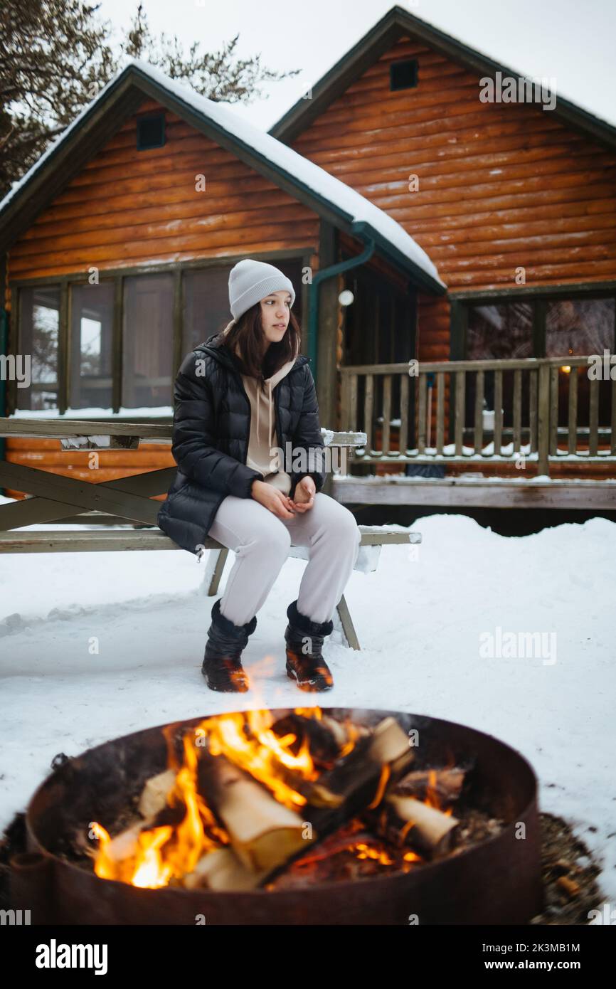 Full body woman in outerwear looking away while sitting on bench near ...
