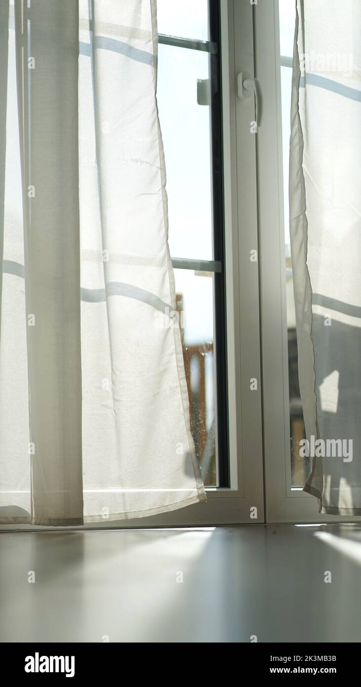 A vertical closeup of mildly waved white curtains in front of a window ...