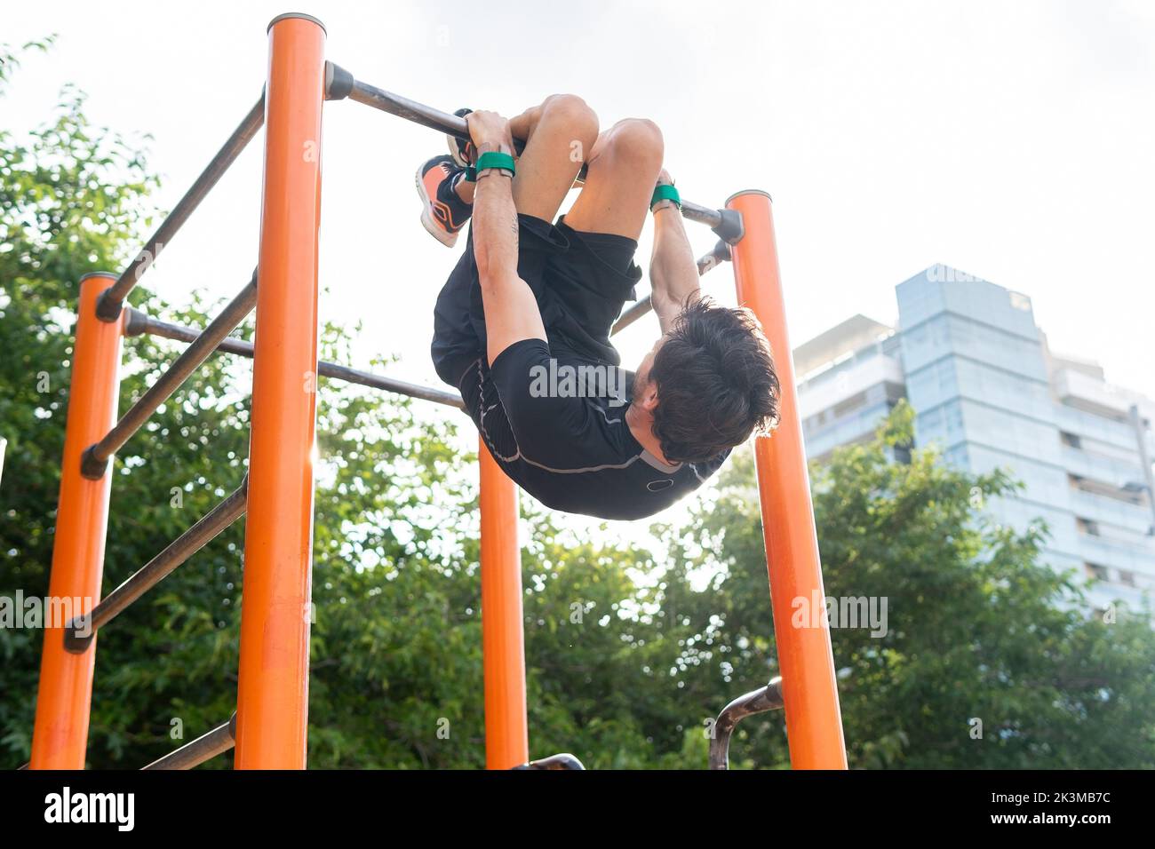 From below anonymous male athlete hanging upside down on bar against cloudy sky during fitness ...