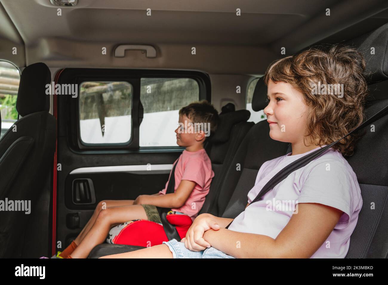 Side view of brother and sister in casual clothes sitting on back seat ...