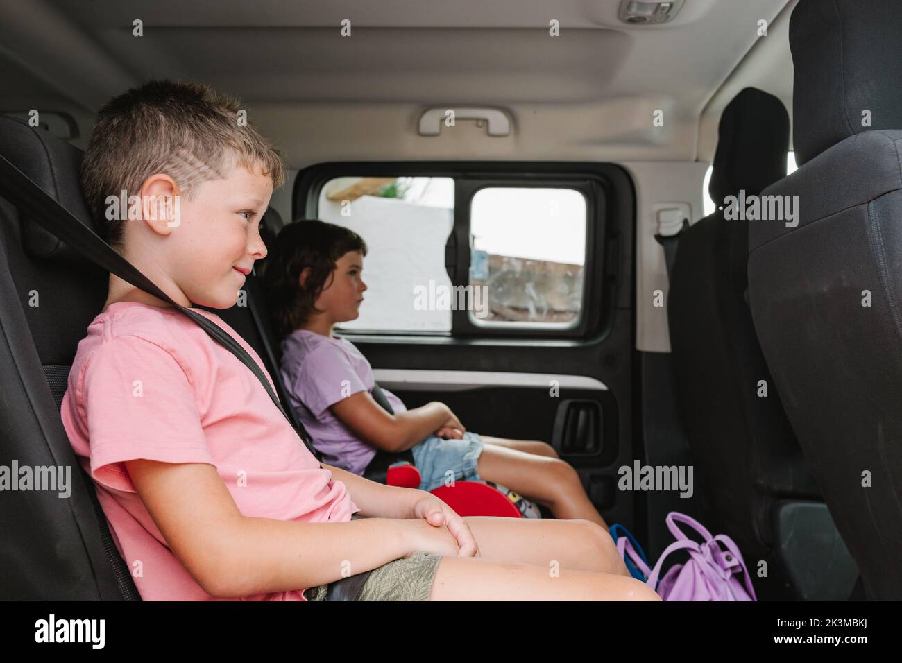 Side view of brother and sister in casual clothes sitting on back seat ...