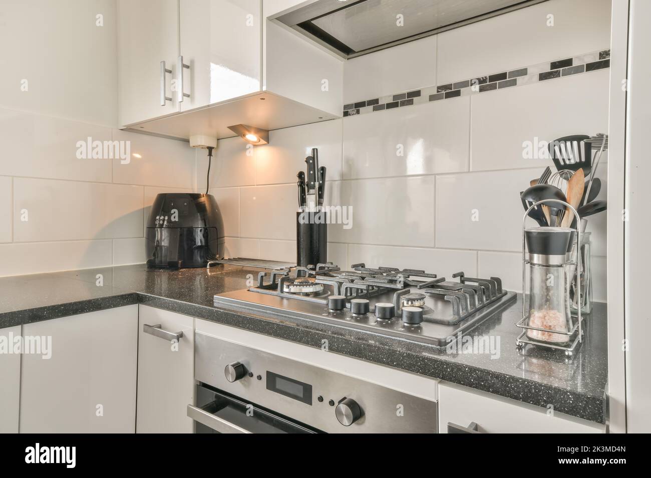 White counter with cooker and utensils placed in light spacious kitchen ...