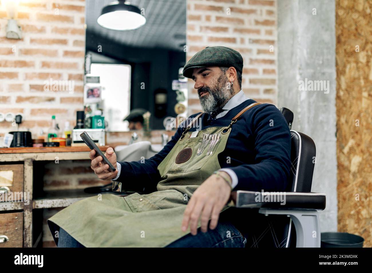 Side view of middle aged male barber sitting on chair in barbershop and ...