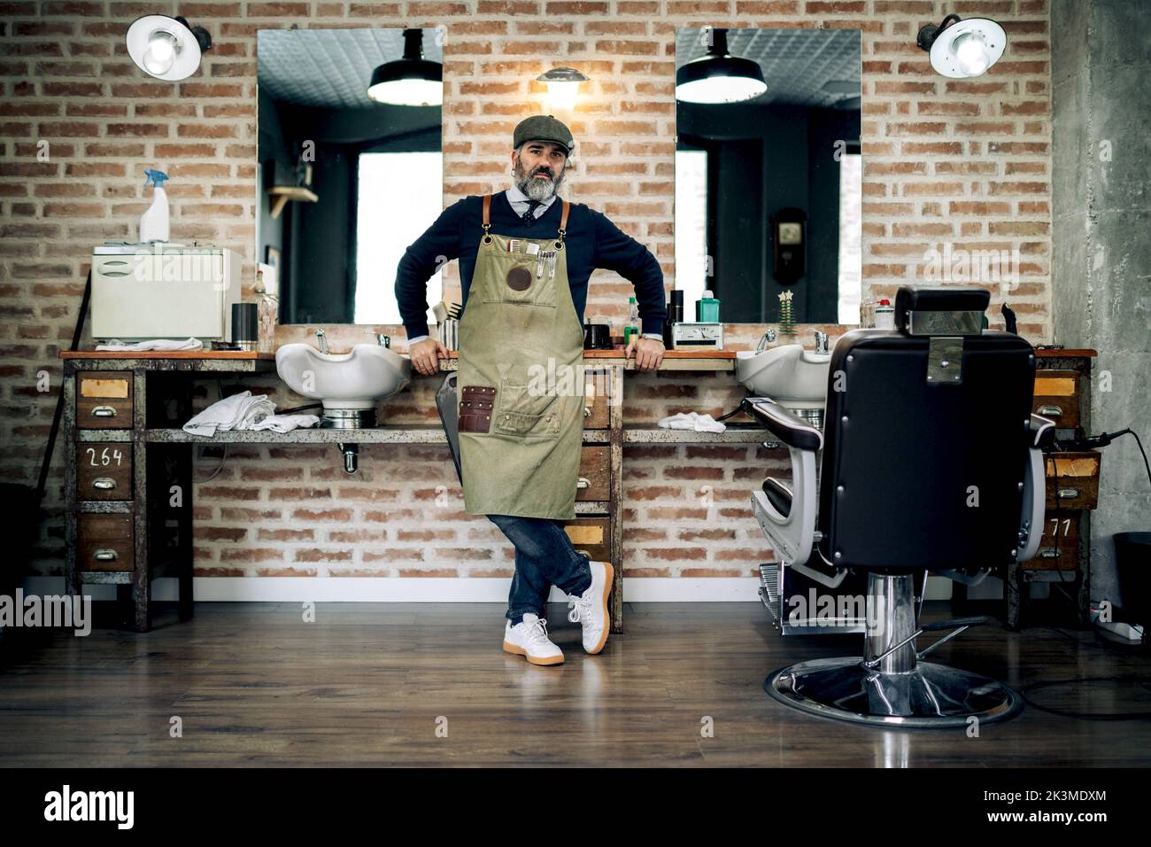 Full body of middle aged male barber in cap and apron standing near ...