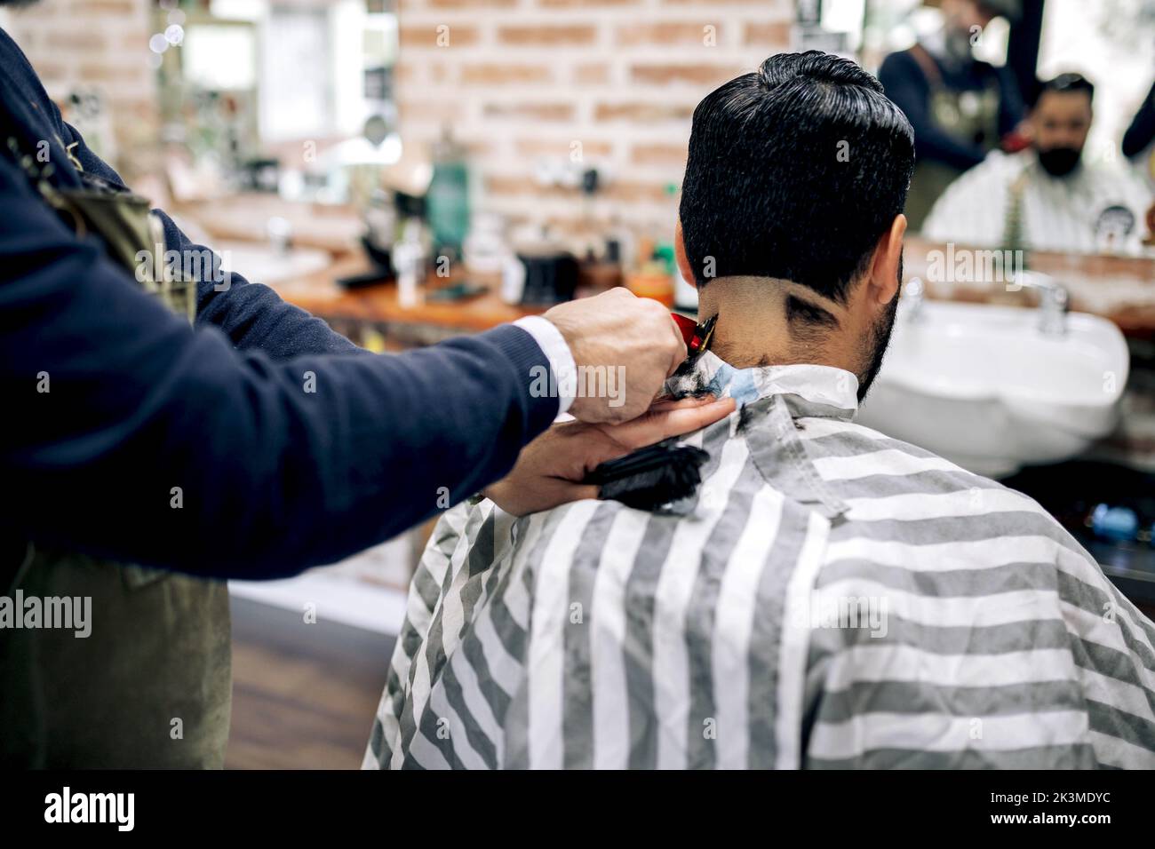 Crop barber using trimmer and cutting hair of male customer in cape ...