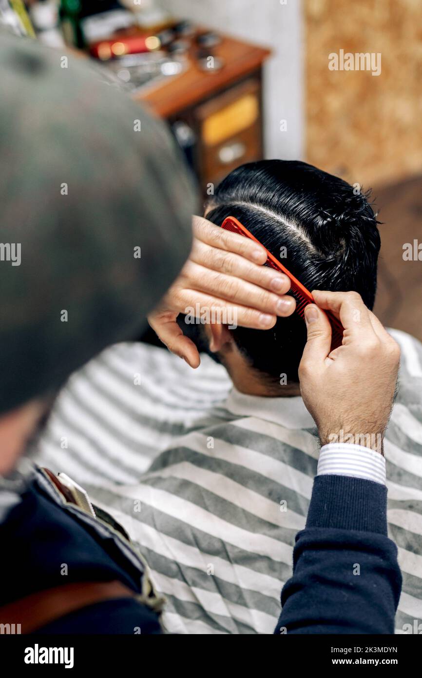 High angle of male barber with comb brushing hair of unrecognizable ...
