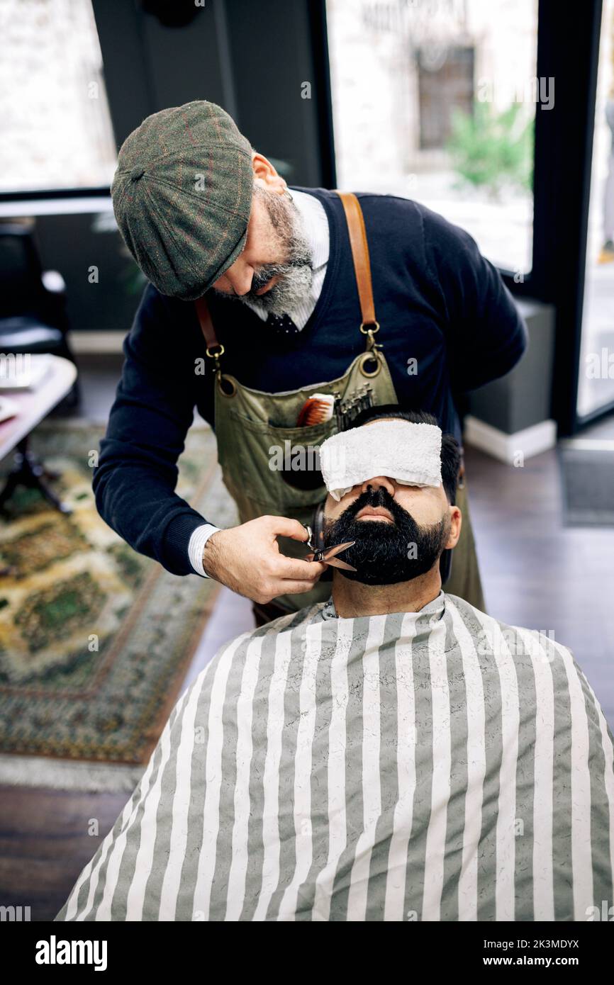 Concentrated middle aged unshaven male barber in apron and beret ...