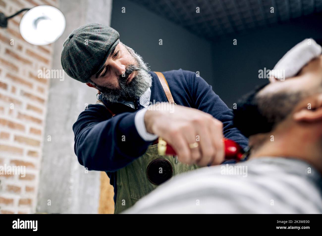Crop unrecognizable barber using electric razor while shaving dark ...