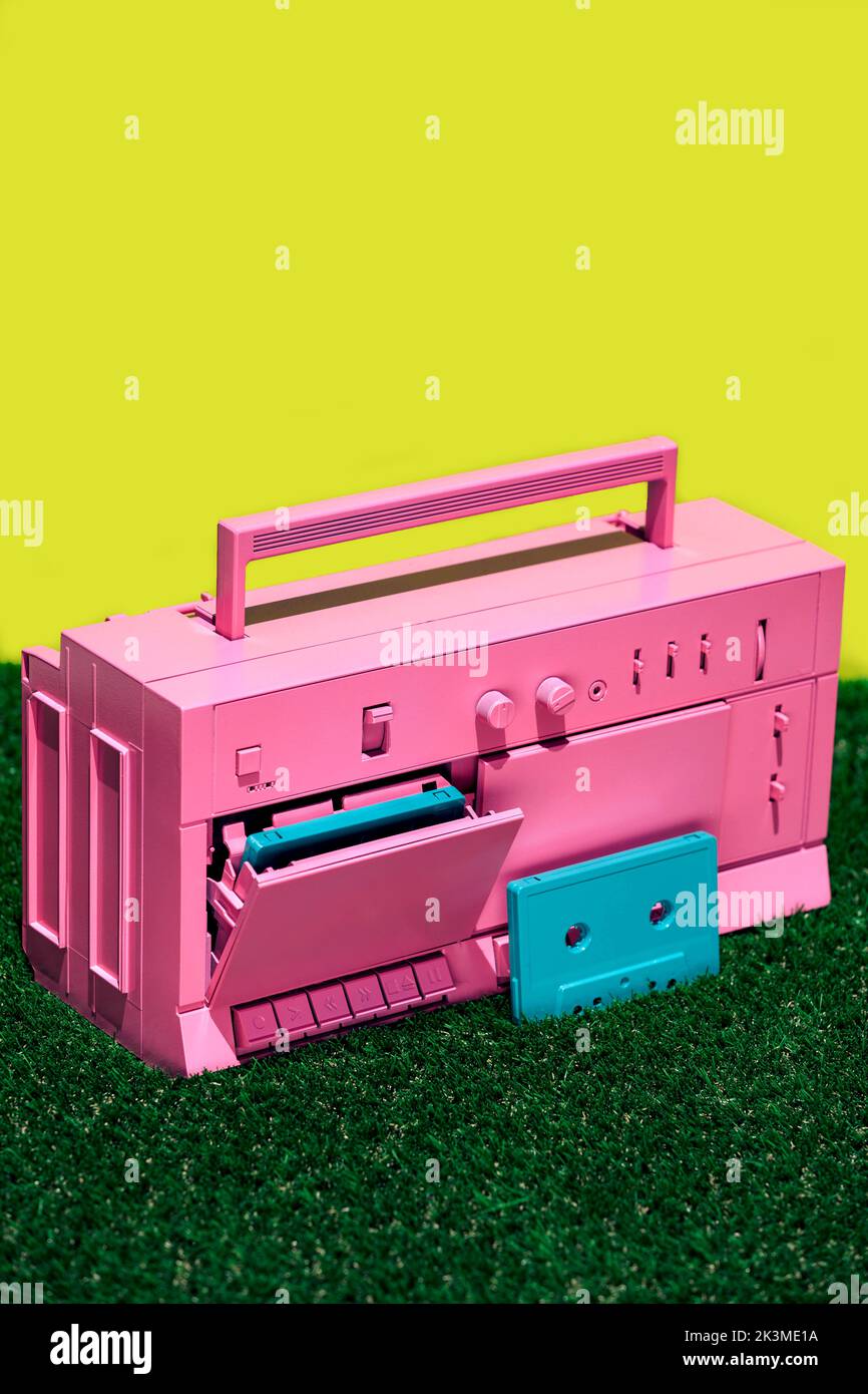 Bright pink vintage cassette player with blue cassettes placed on green ...