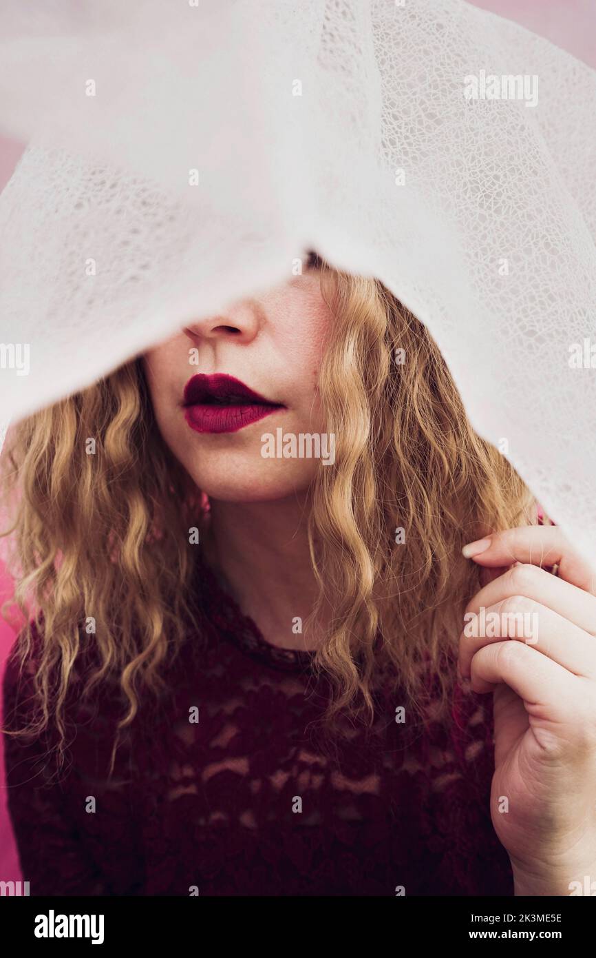 Young unrecognizable sad female with red lips hiding behind veil ...