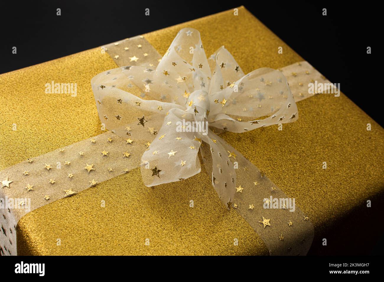 Gift box in a golden wrapper with a bow close-up on a black background ...