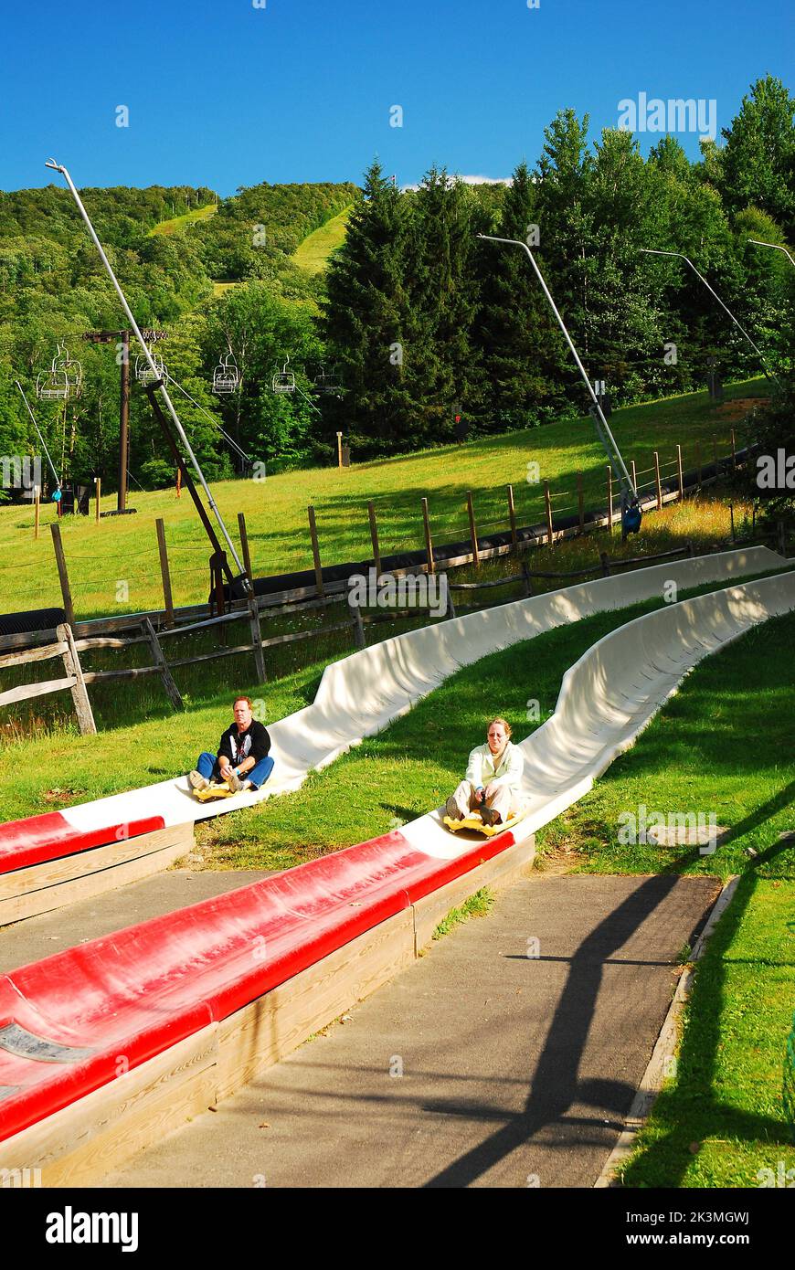 An adult man and woman rush downhill on an alpine slide ride at a ski ...