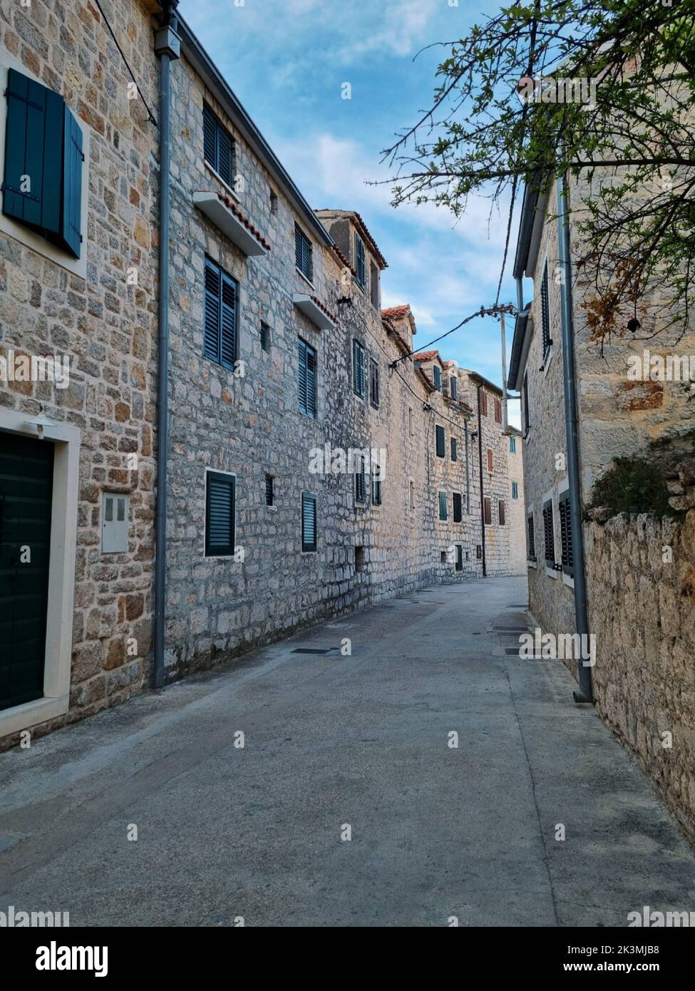 A vertical shot of concrete alley between rows of old stone buildings ...