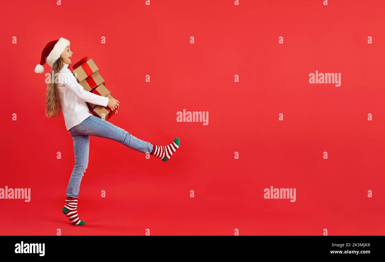 Happy little girl carrying stack of Christmas presents on red copy ...