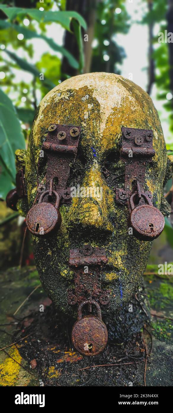A vertical shot of an old mysterious mossy statue with a locked mouth ...