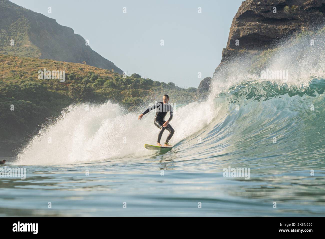 A young male surfer surfs on a large empty breaking wave in front of ...