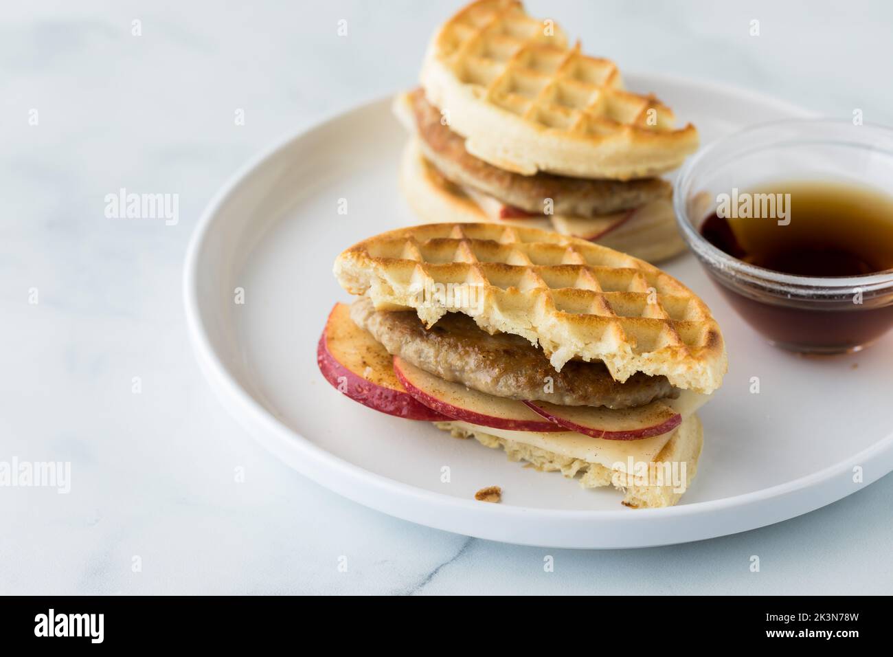 A toasted waffle and sausage sandwich served with maple syrup for ...