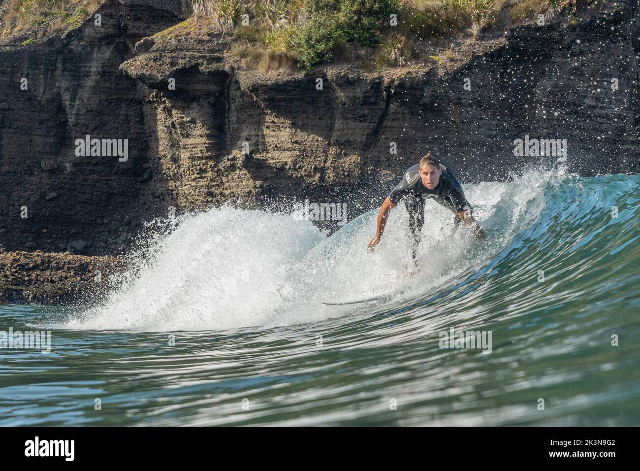 A young male surfer surfs on a large empty breaking wave in front of ...