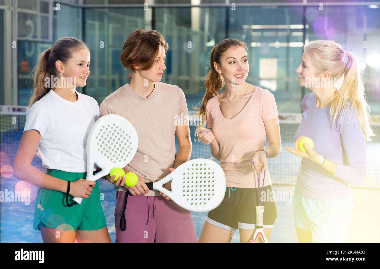 Teenage boy, girl and adult women standing in padel court and talking ...
