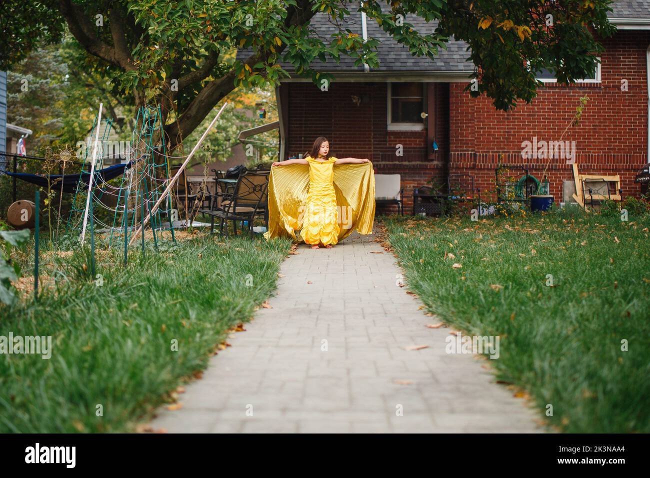 Distant-view of child in flowing cape and dress walking through garden ...