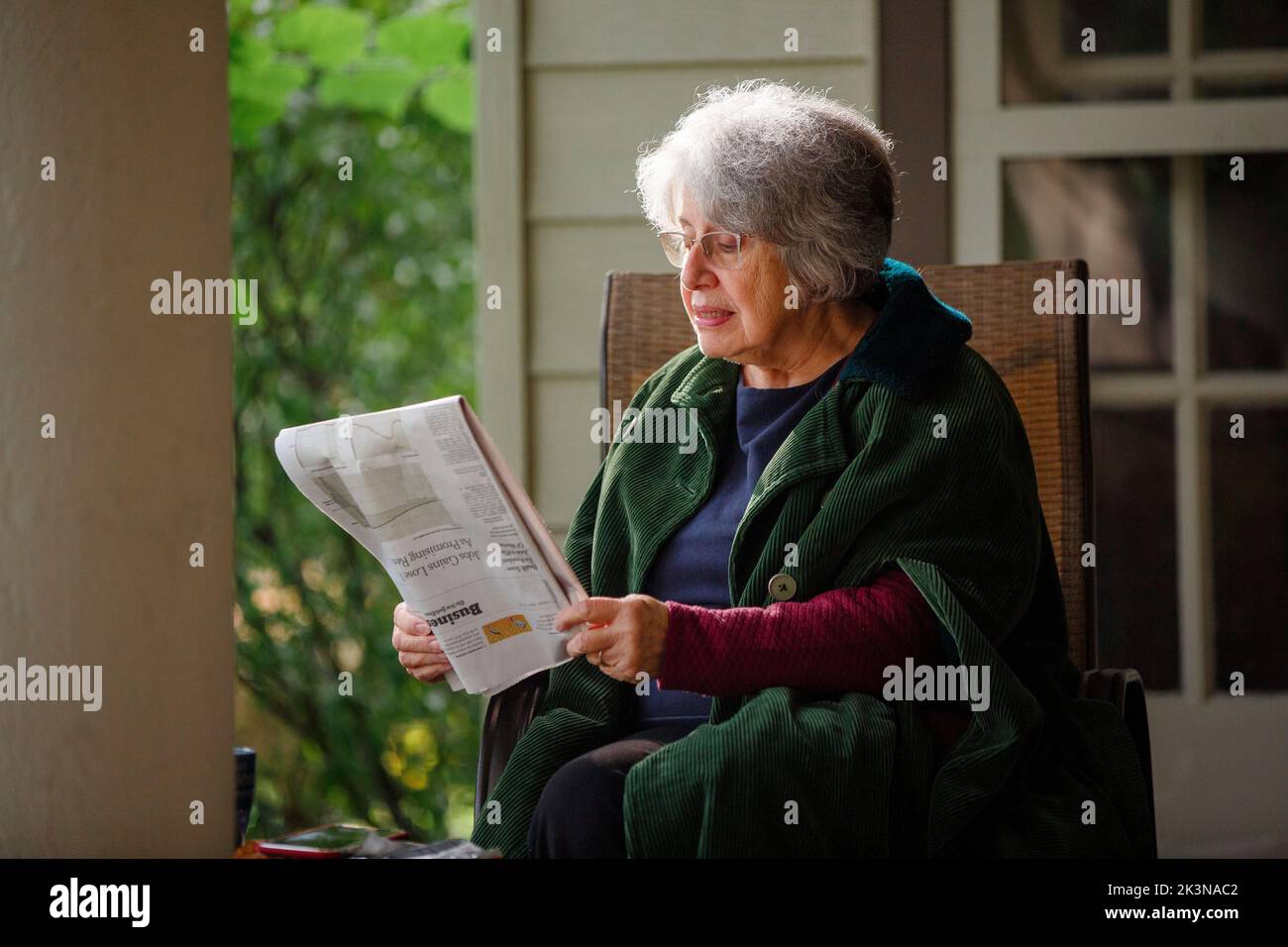 An elderly woman sits on front porch in cloak reading newspaper Stock ...