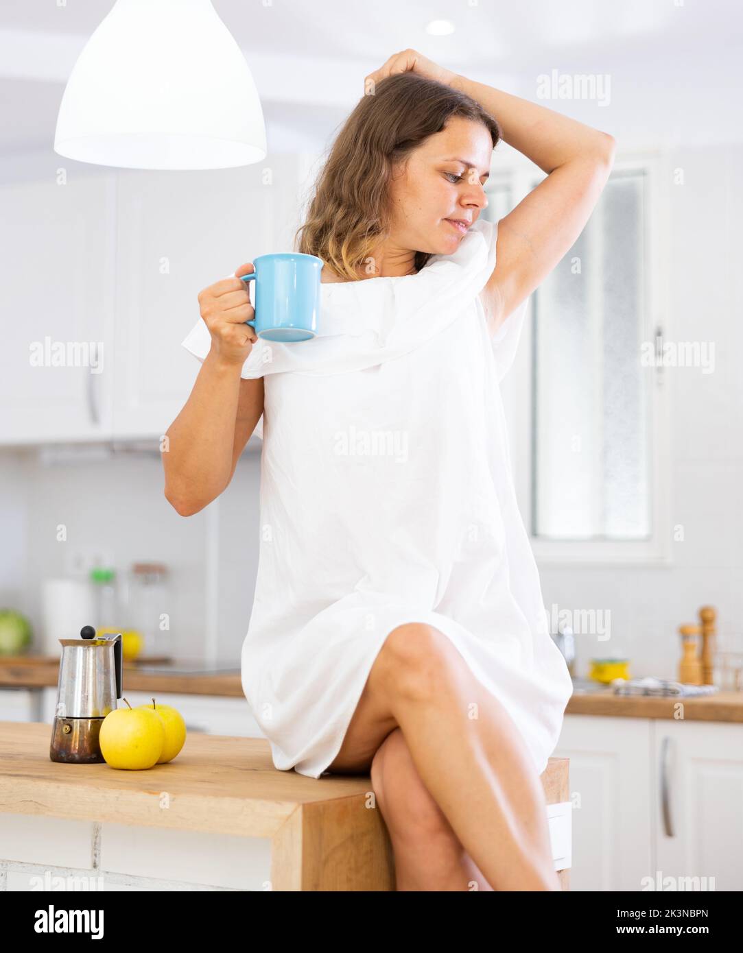 Woman sitting on kitchen countertop, drinking coffee Stock Photo - Alamy