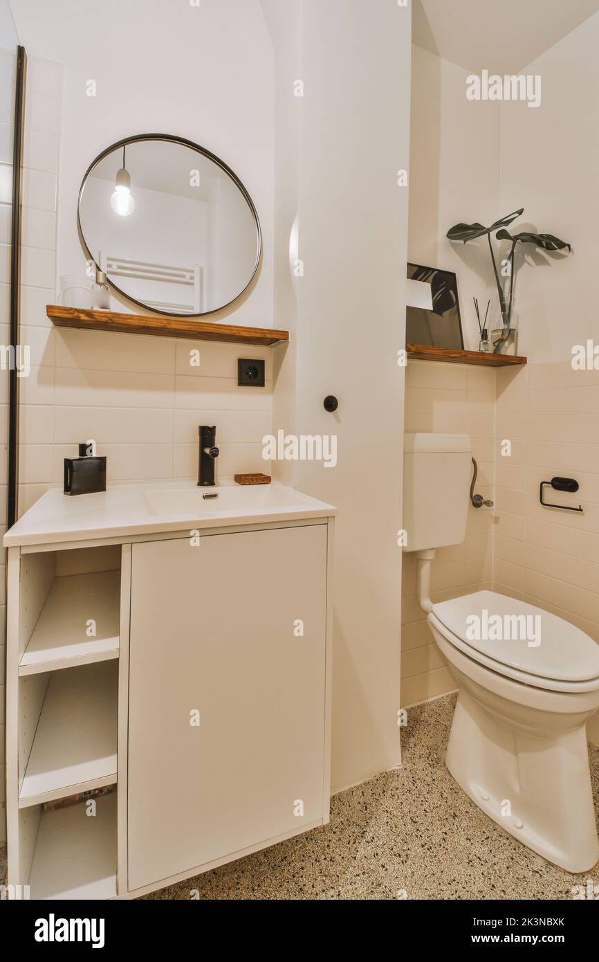 Flush toilet located between sink and shower in small tiled bathroom of ...