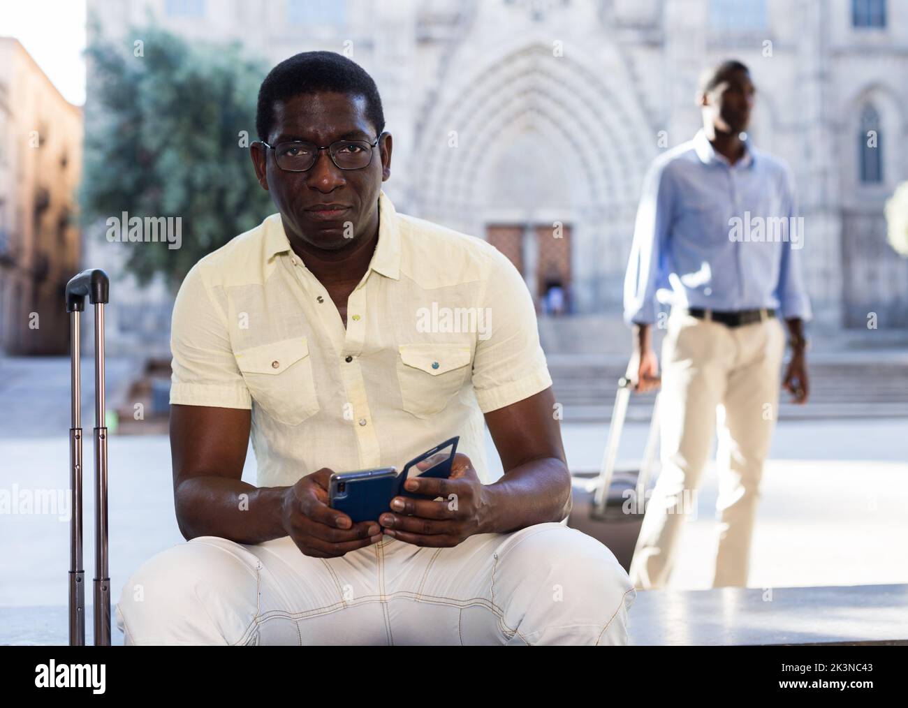 African American traveler sitting on bench with mobile phone Stock ...