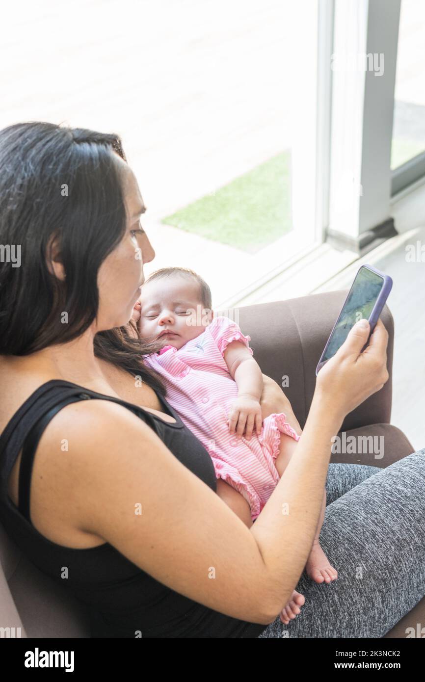 vertical photo of a mother working on her cell phone with her baby in ...