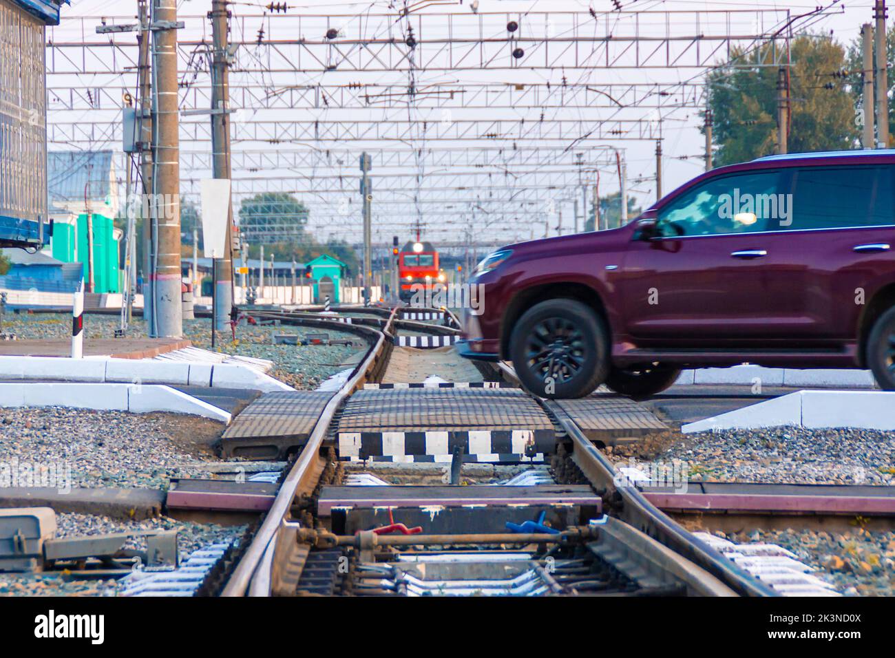 a red locomotive is approaching the railway crossing, an all-terrain ...