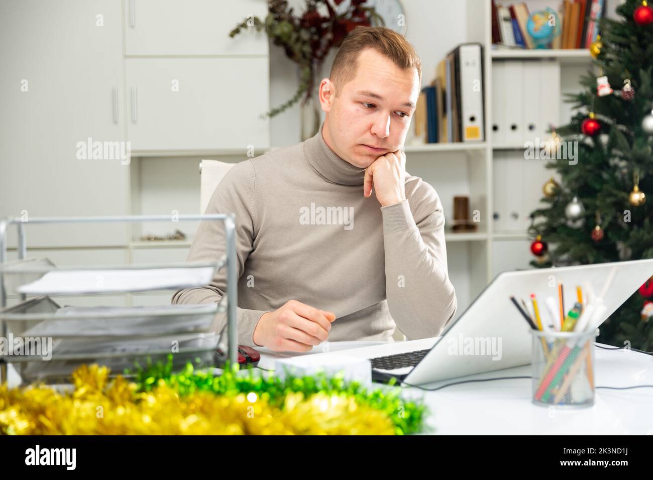 Exhausted male office worker sitting at his desk in Christmas decorated ...