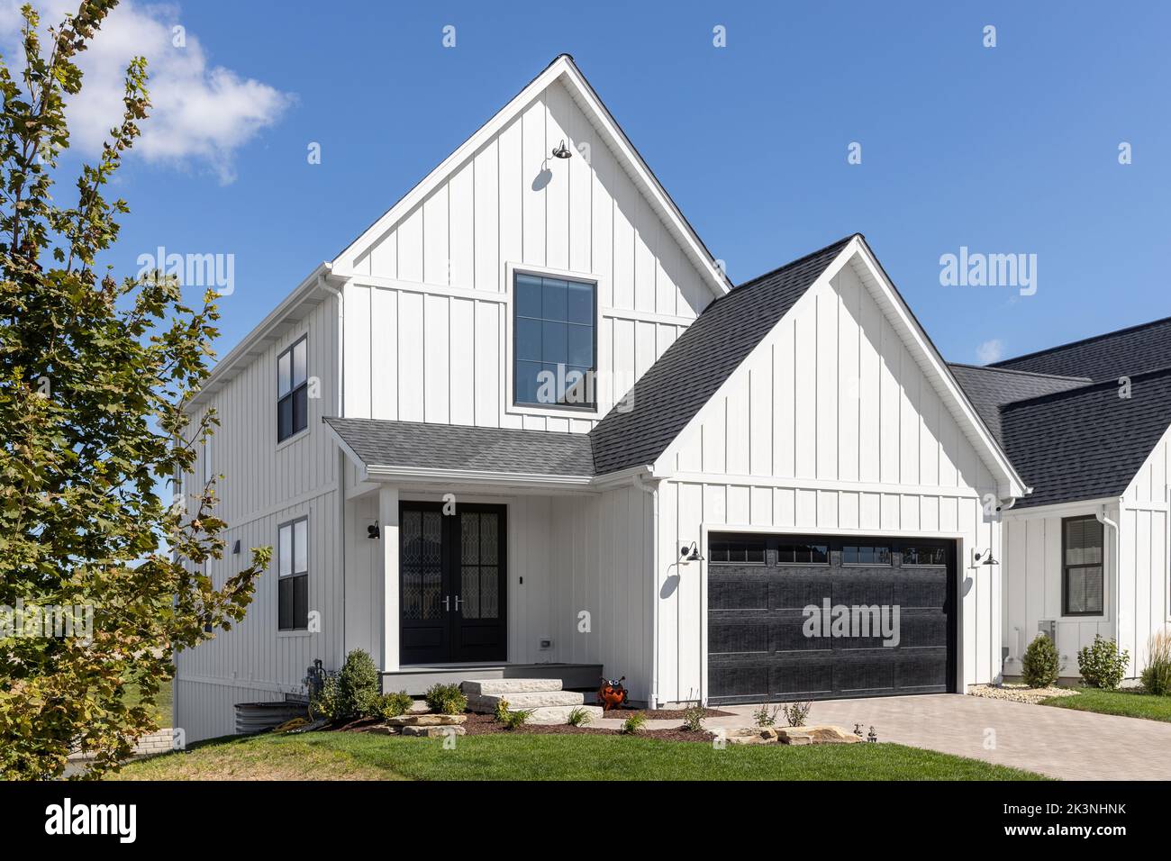A large, white modern farmhouse with vertical siding, a black two car ...