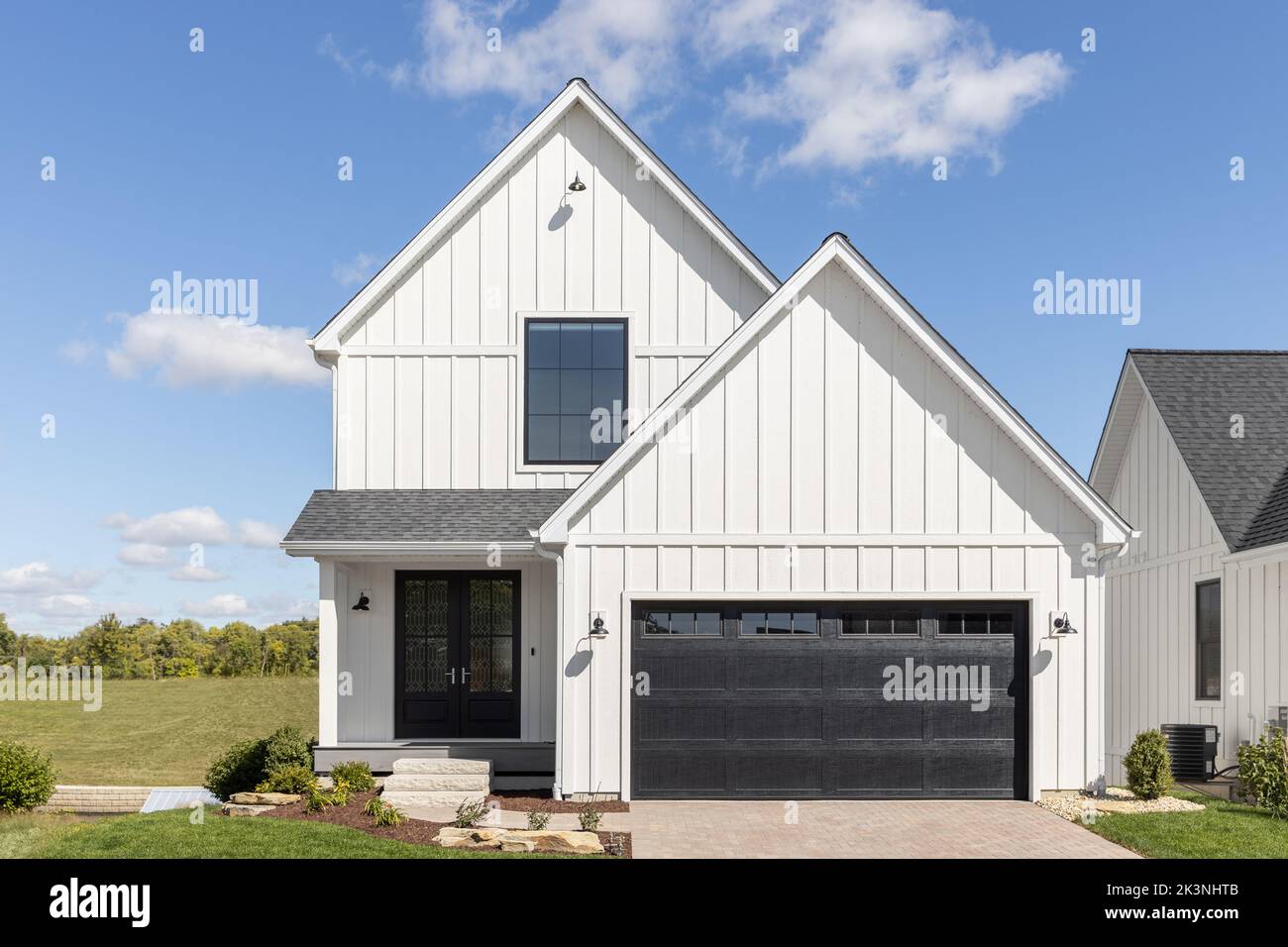A large, white modern farmhouse with vertical siding, a black two car ...