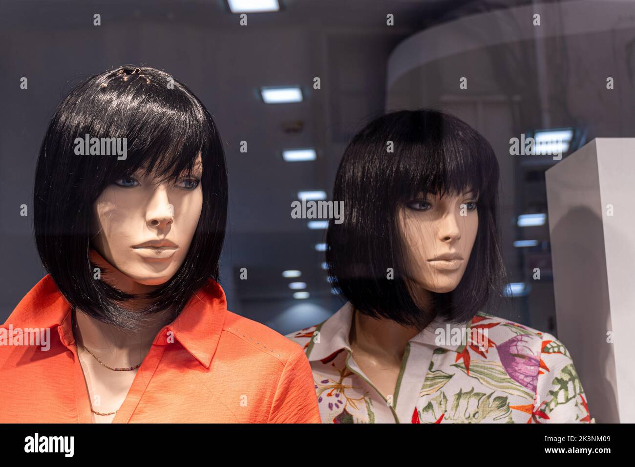 Two realistic female mannequins with black short wigs behind the glass ...