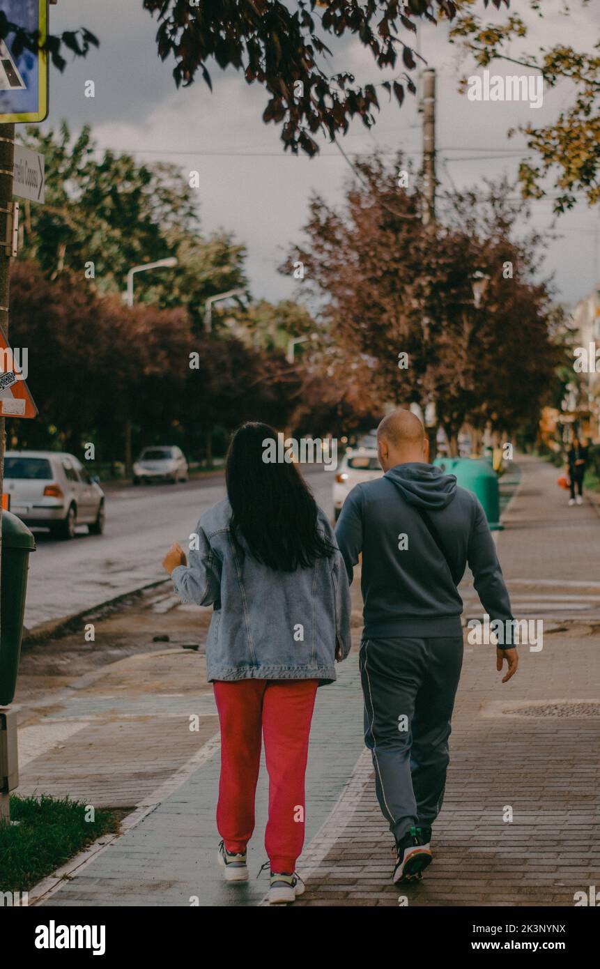 A vertical closeup shot of two people walking on the street on a sunny ...