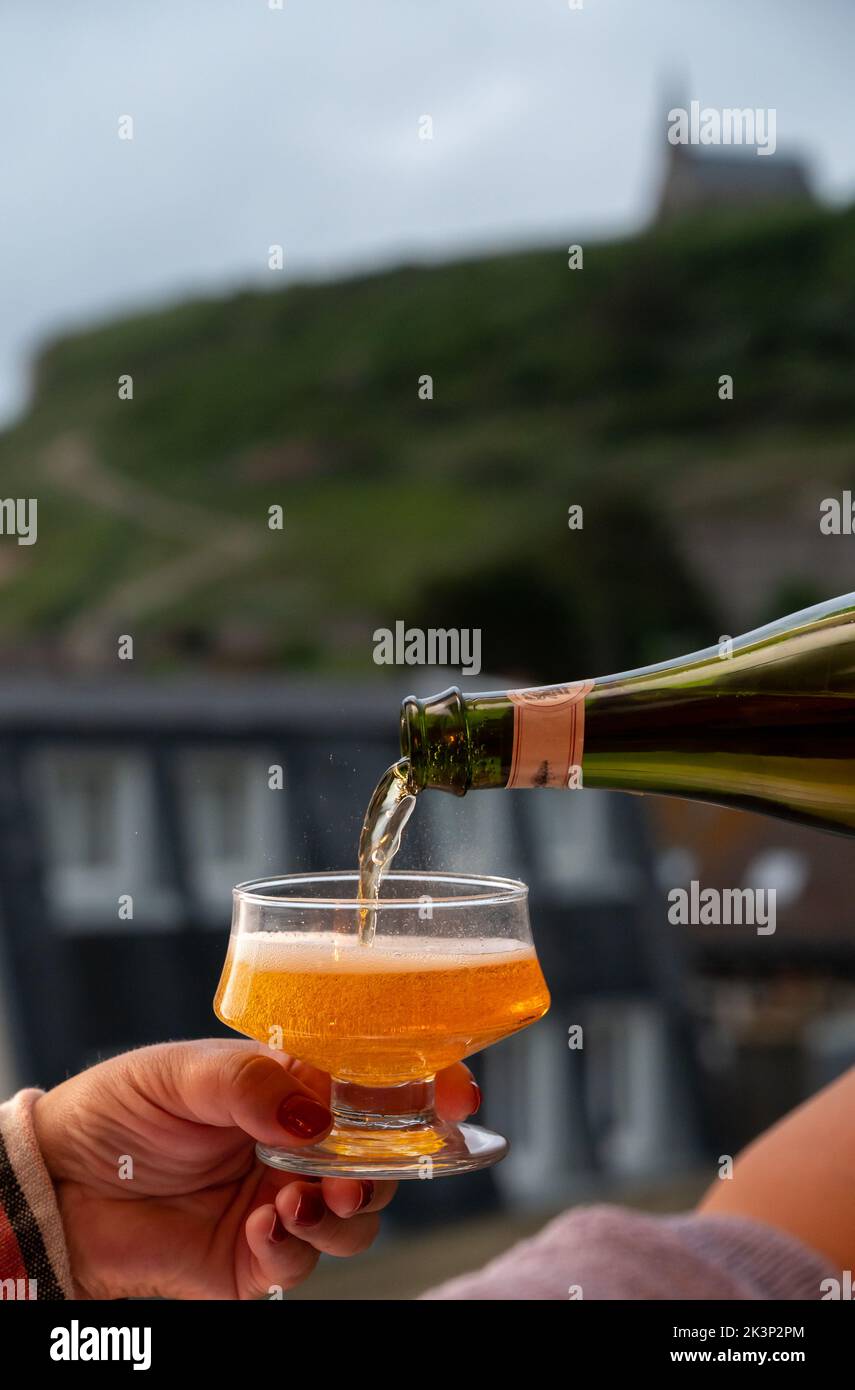Pouring of tasty apple cider drink in glass with houses of Etretat ...