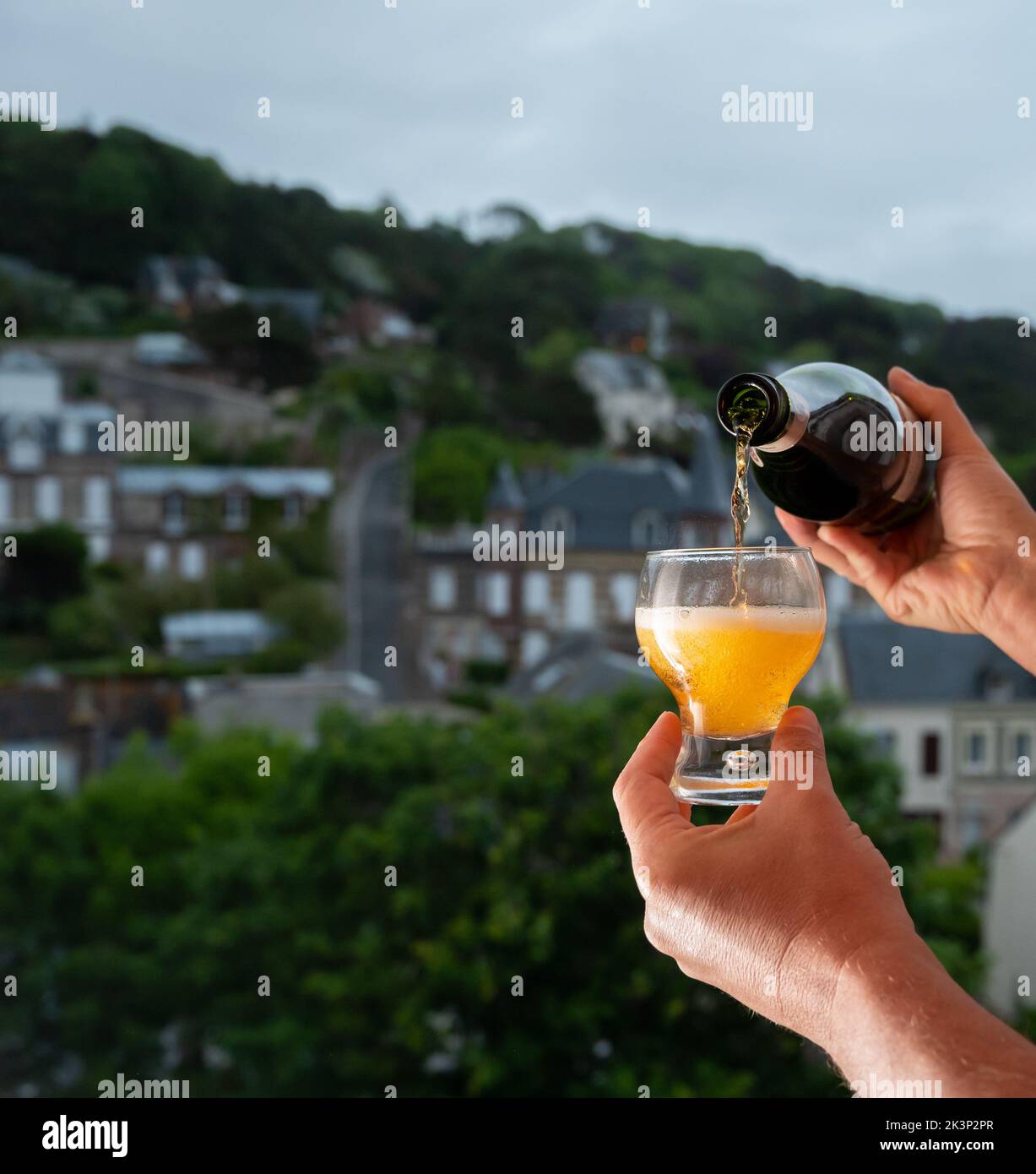 Pouring of tasty apple cider drink in glass with houses of Etretat ...