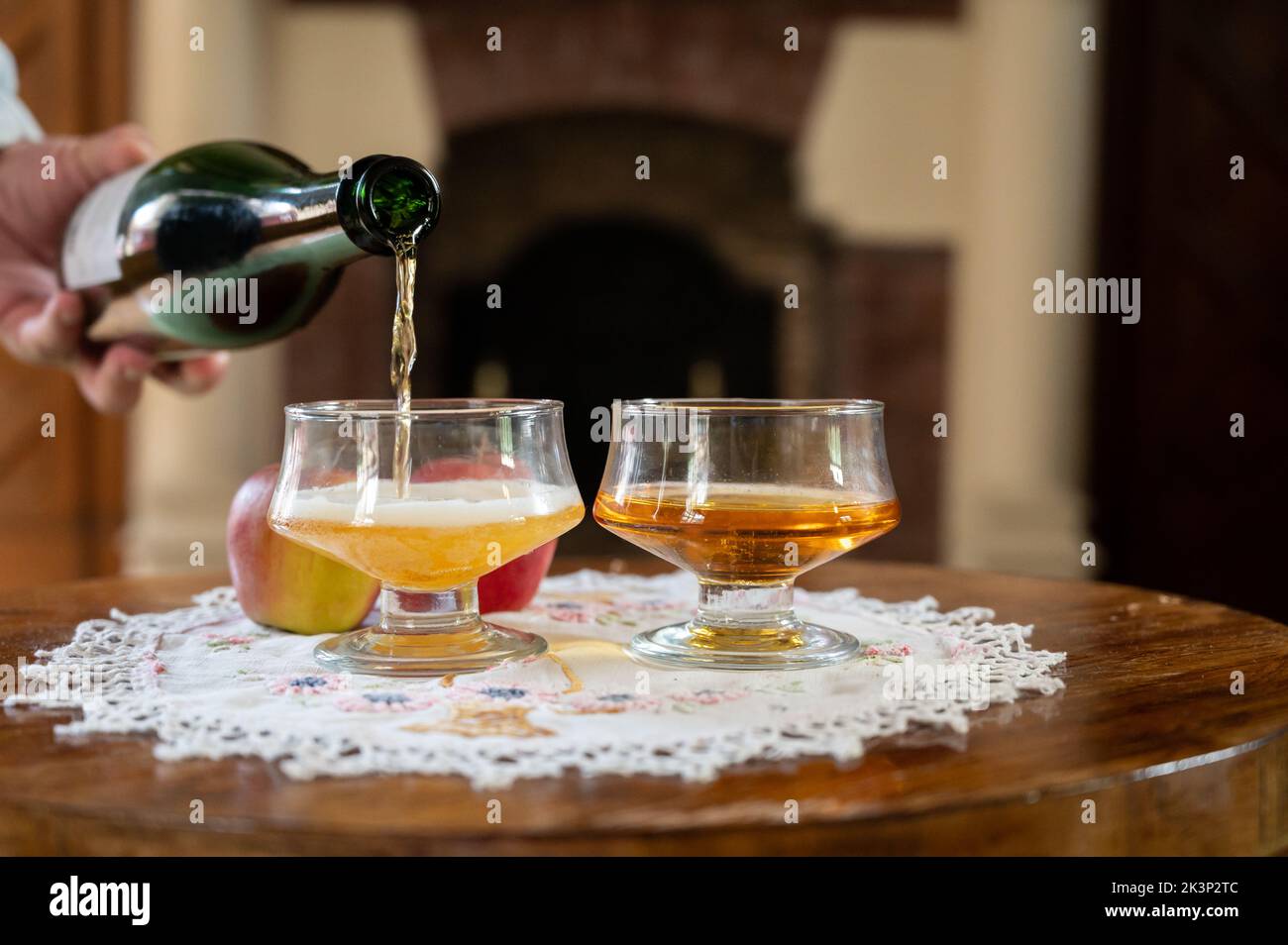 Pouring of apple cider drink in two glasses in old french house with ...