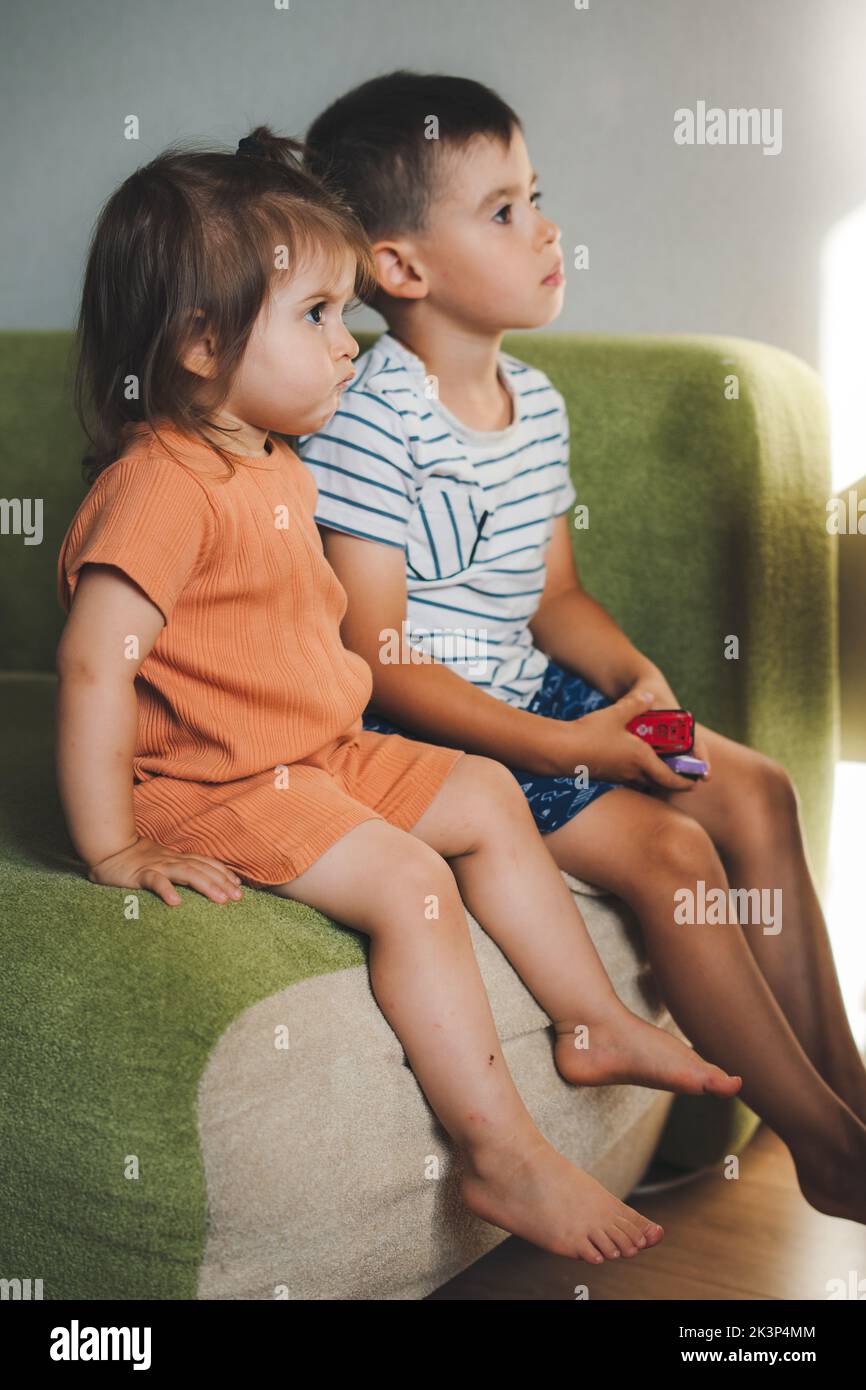 Excited small brother and sister sitting on sofa watching TV in living ...